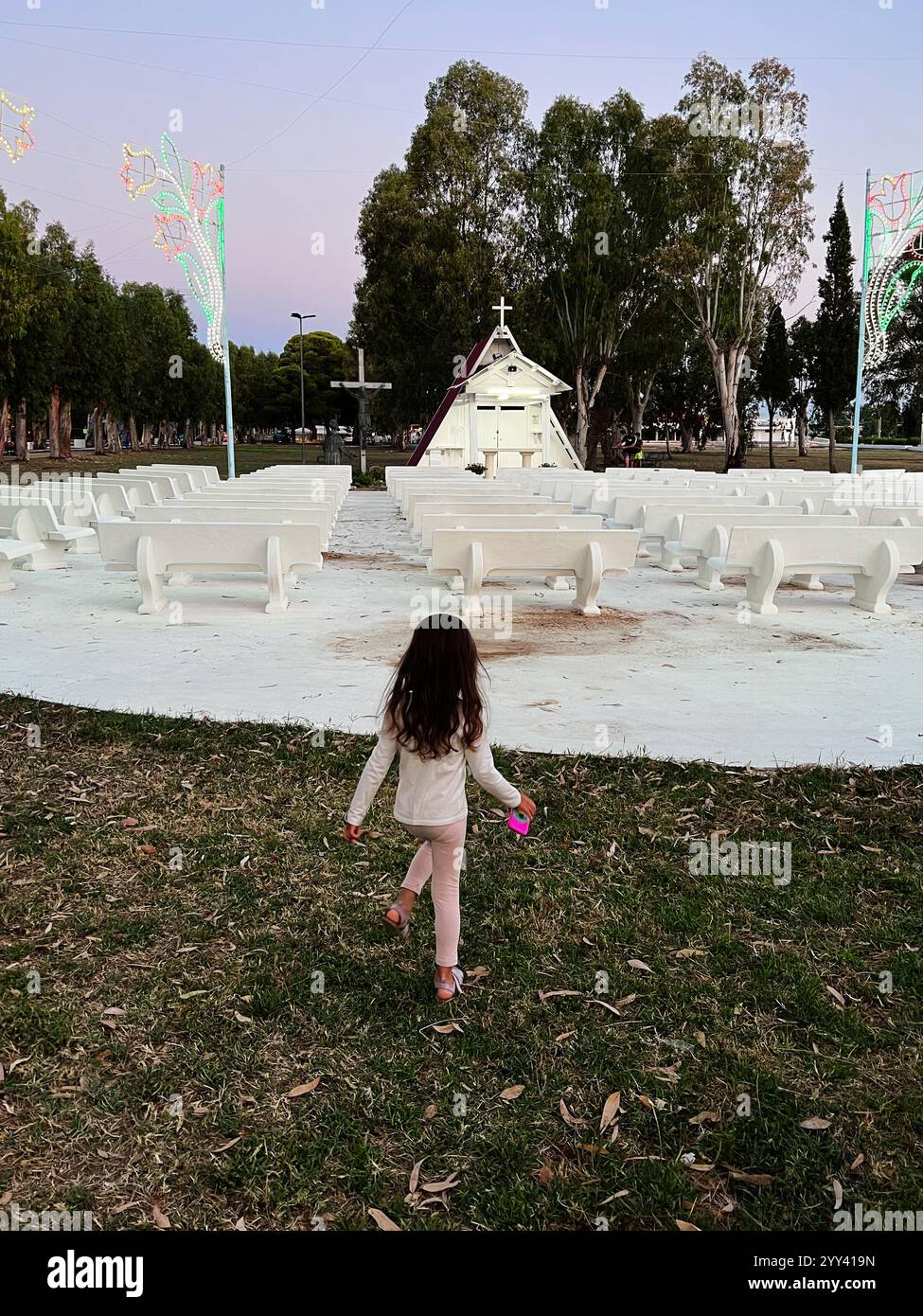 A young girl walks towards an outdoor chapel with white benches ...