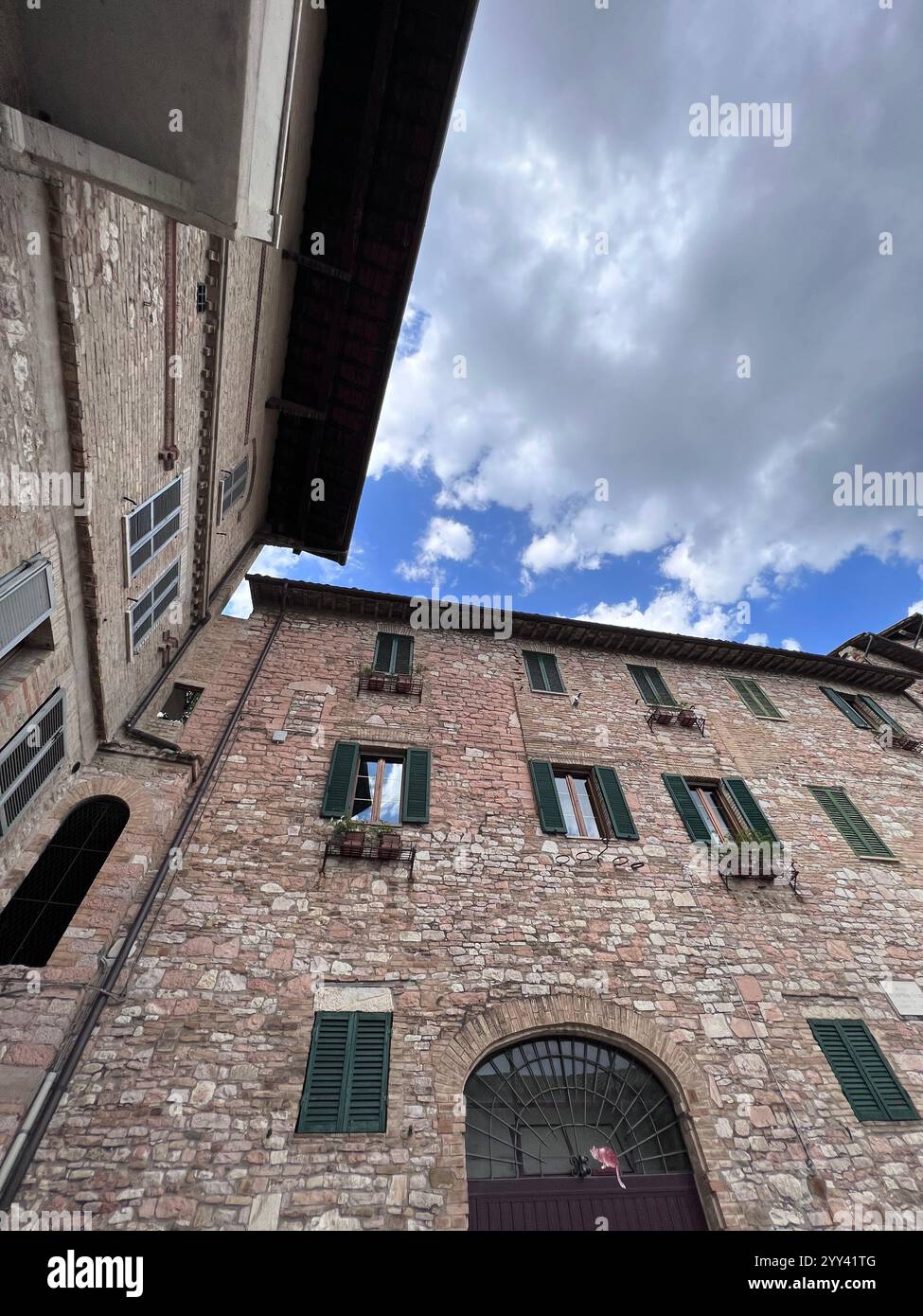 A rustic stone building featuring green shutters is captured from below ...