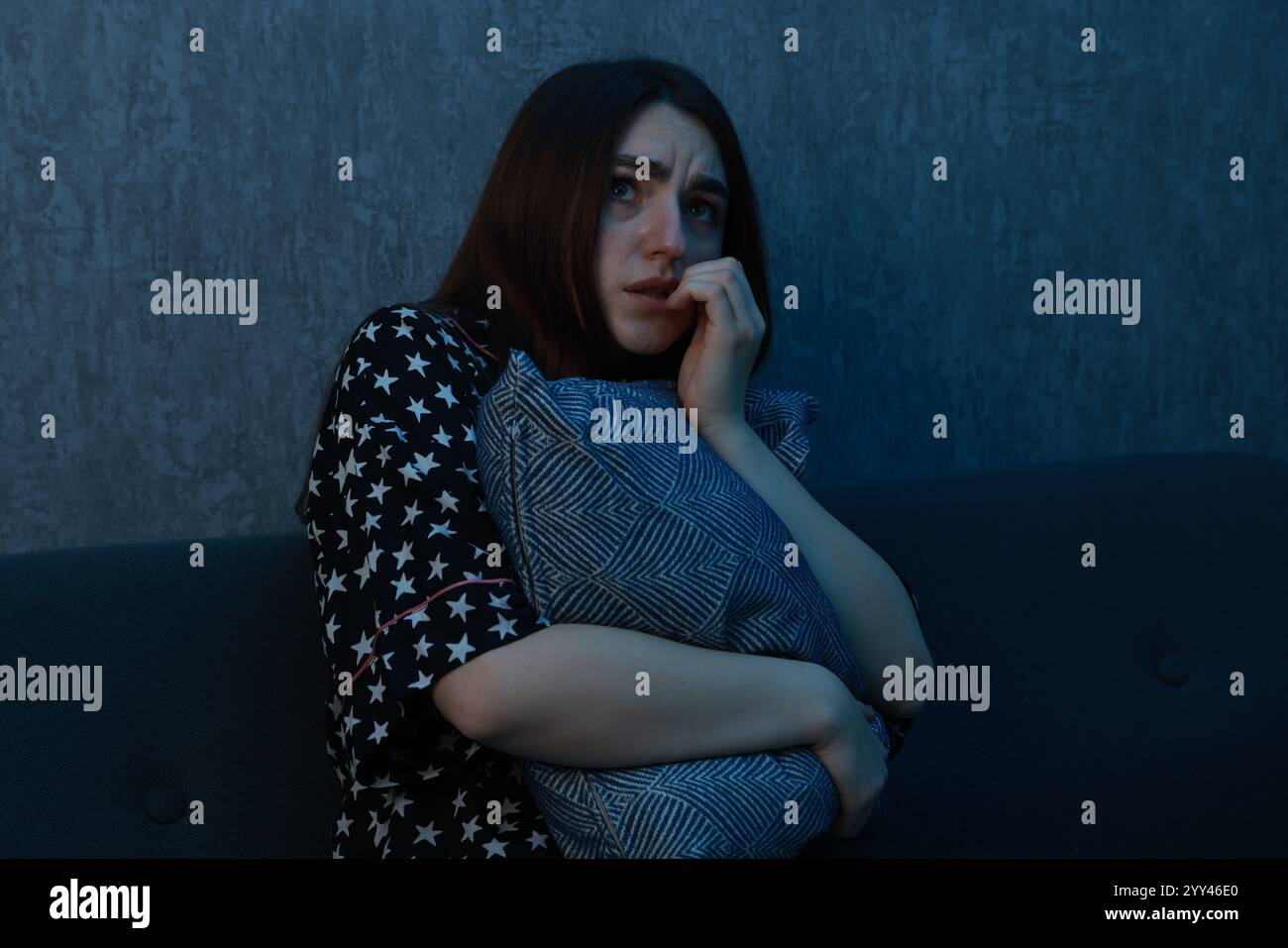 Fear of darkness. Scared young woman hugging pillow on couch indoors at ...