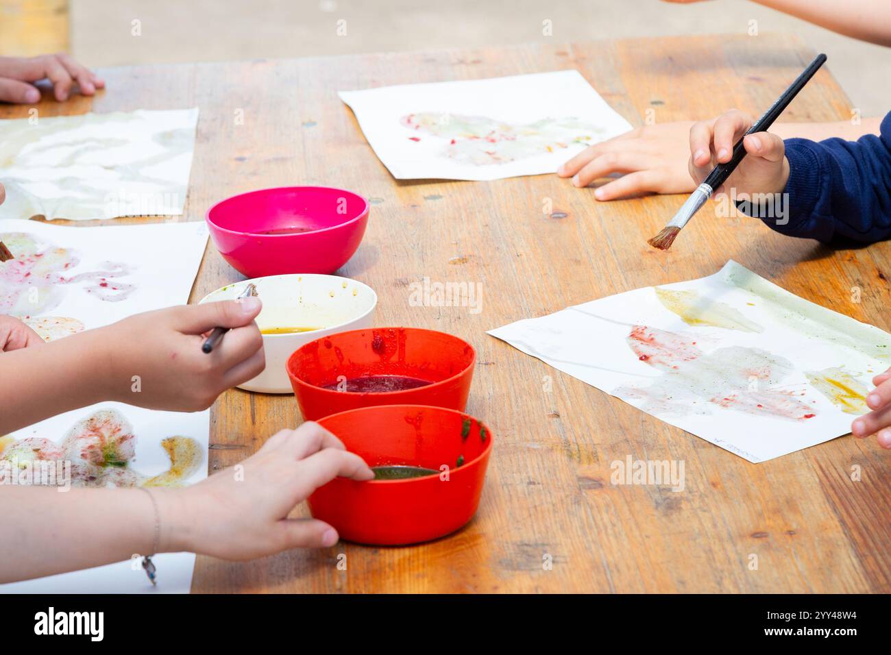 Children sit at a table painting with red bowls of paint Stock Photo ...