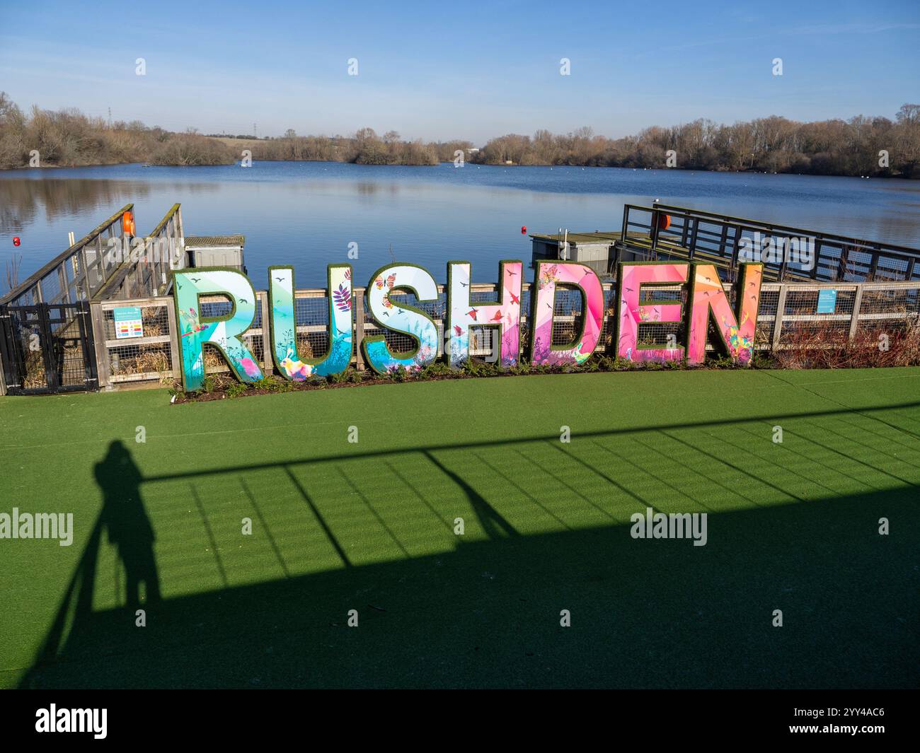 Colourful signage for Rushden Lakes nature reserve with shadow of ...