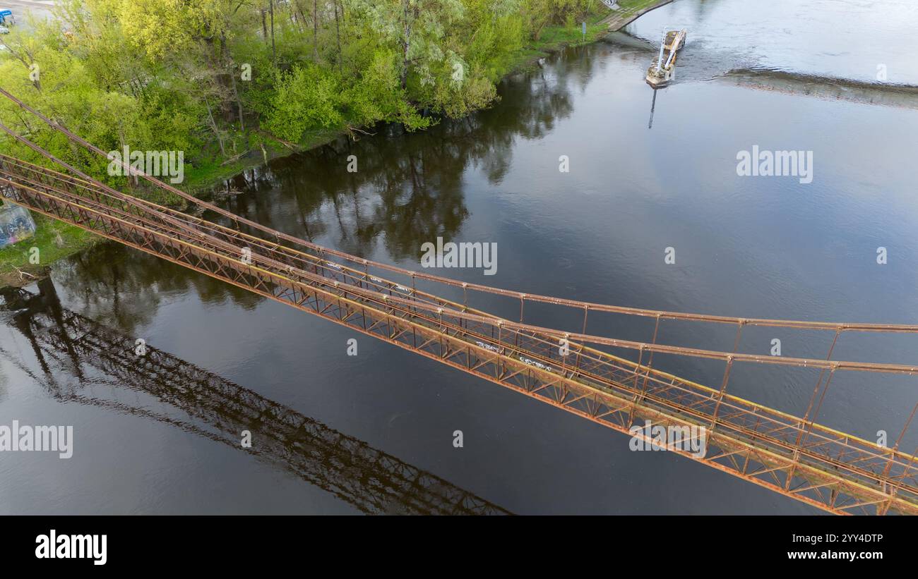 An old industrial pipe bridge crossing a river, surrounded by lush ...