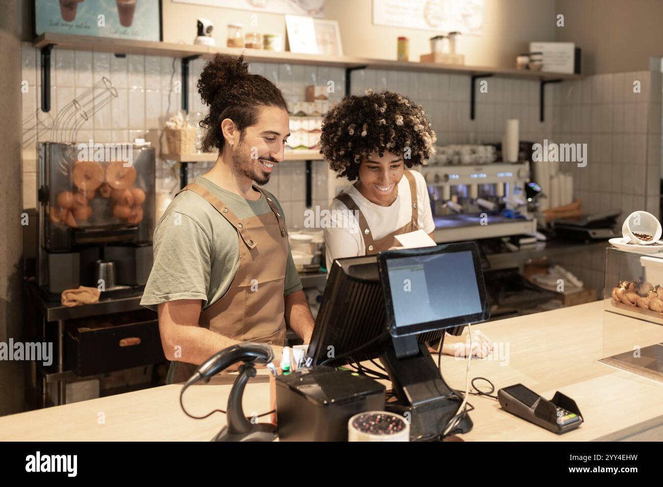 Two cheerful baristas in aprons work together at a cafe counter ...