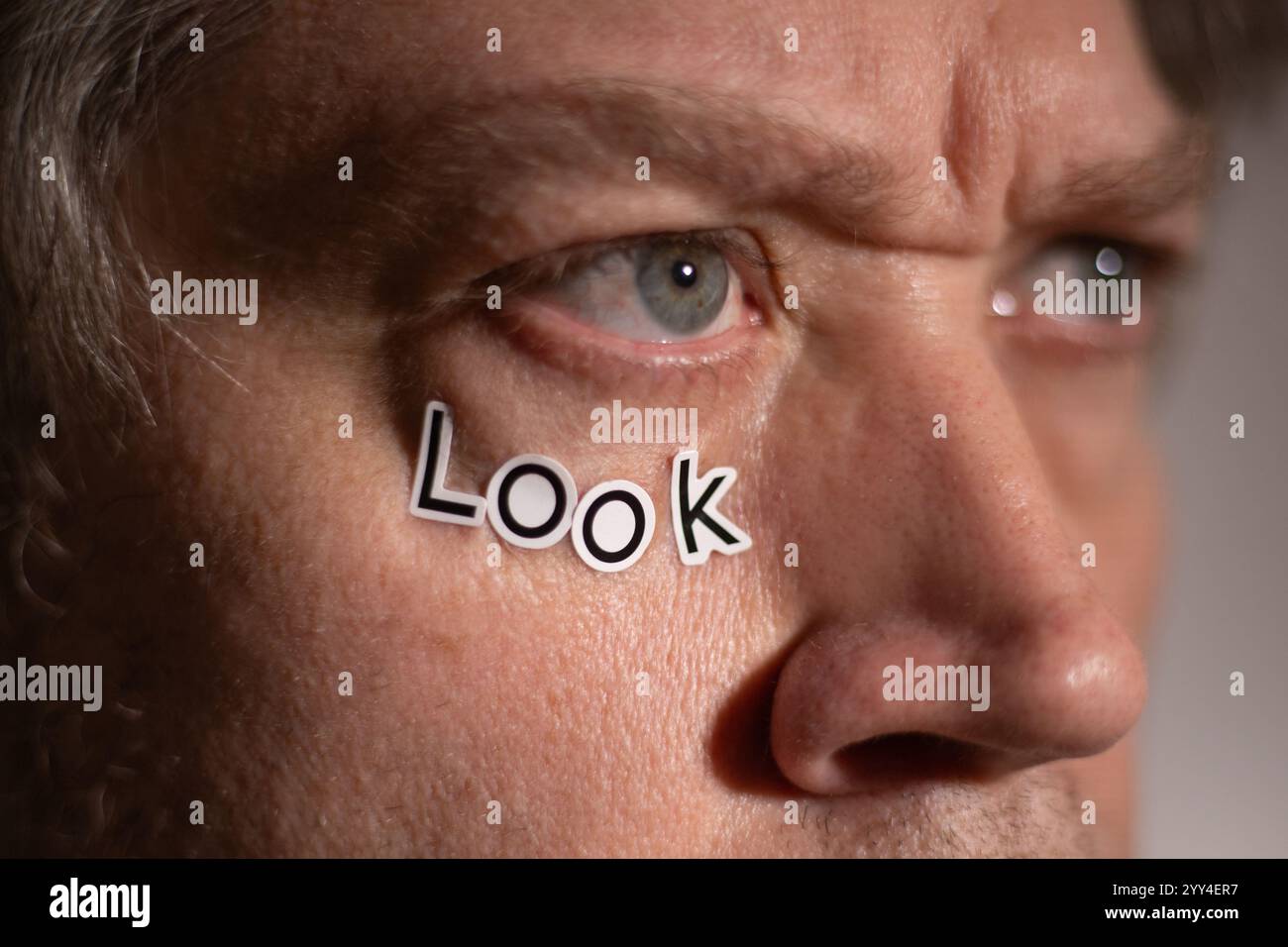 A close-up of a man's face with the word Look spelled out in cut-out ...