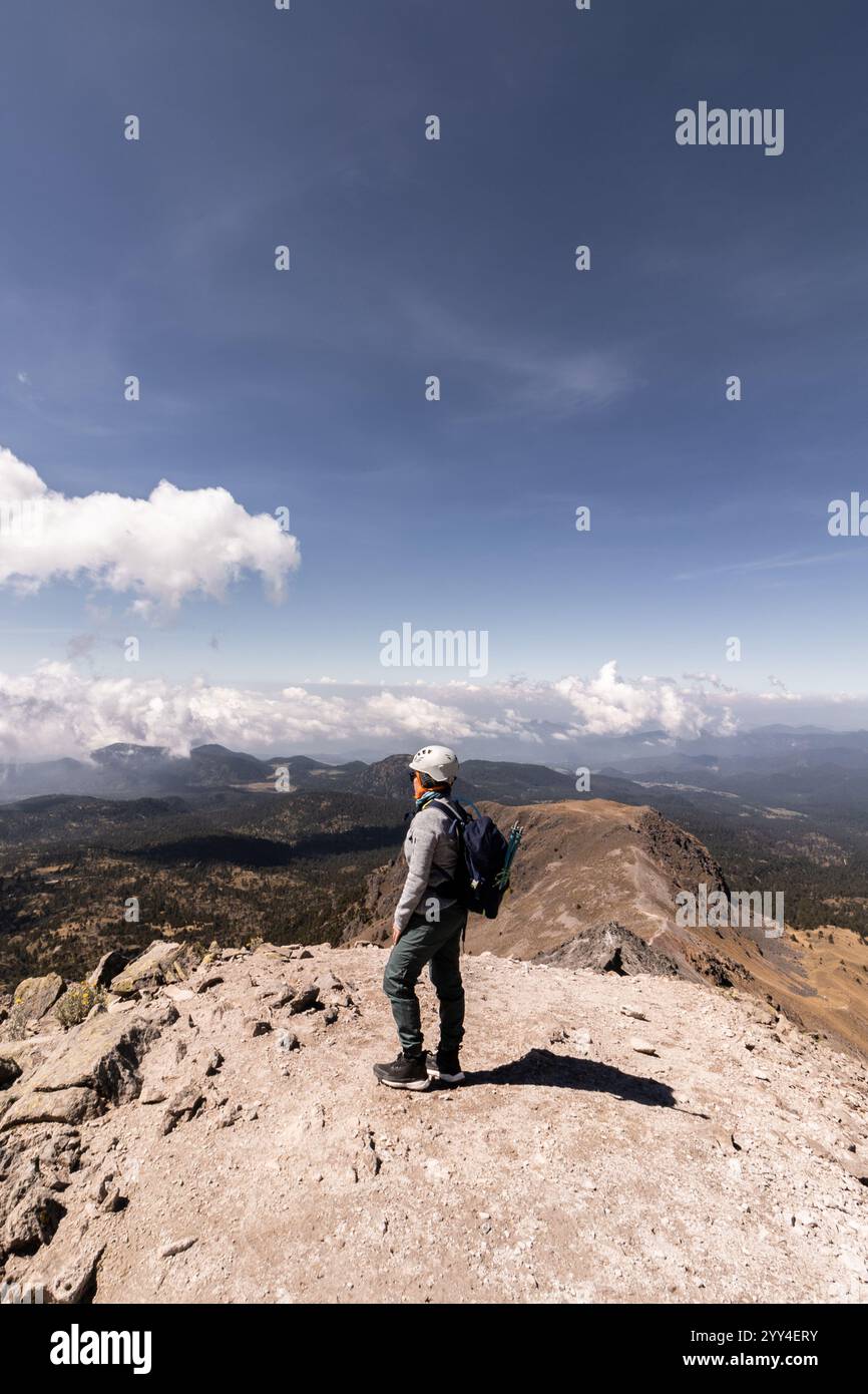 A hiker, equipped with a backpack and helmet, stands on a rocky ...