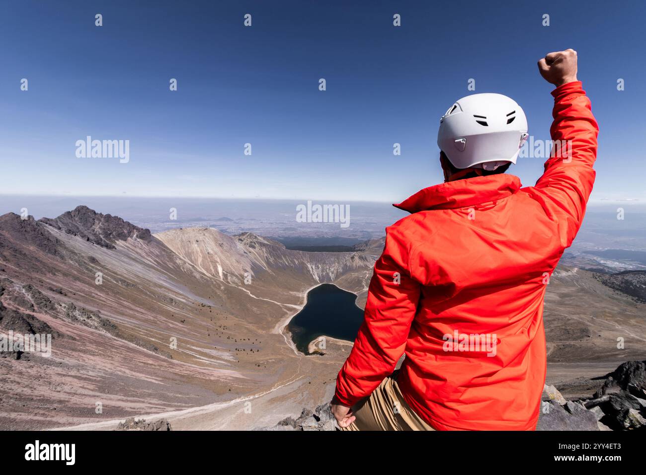 A hiker in a red jacket and helmet celebrates reaching a mountain ...