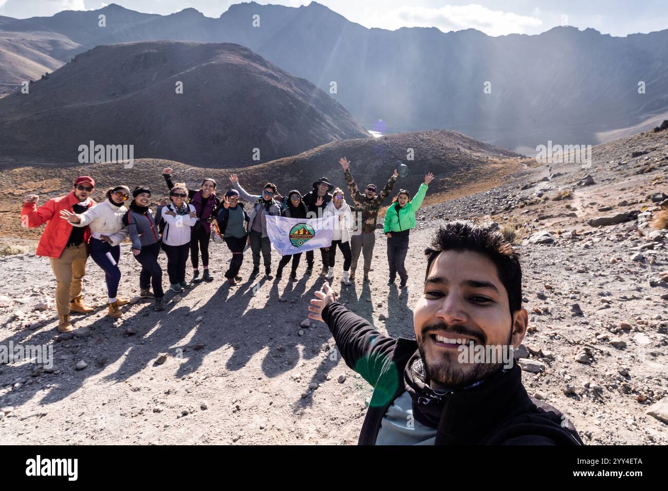 A cheerful group of hikers takes a selfie at a mountain summit ...