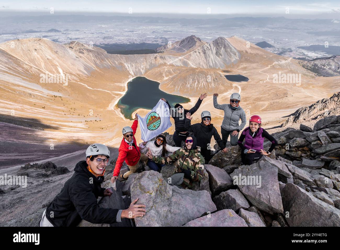 A group of hikers celebrates at a mountain summit, displaying a flag ...
