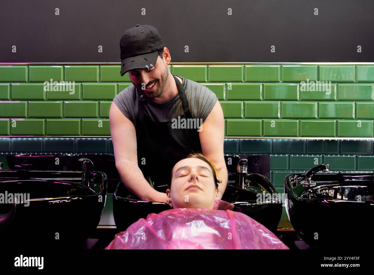 A hairstylist in a cap and apron washes a customer's hair in a sleek ...