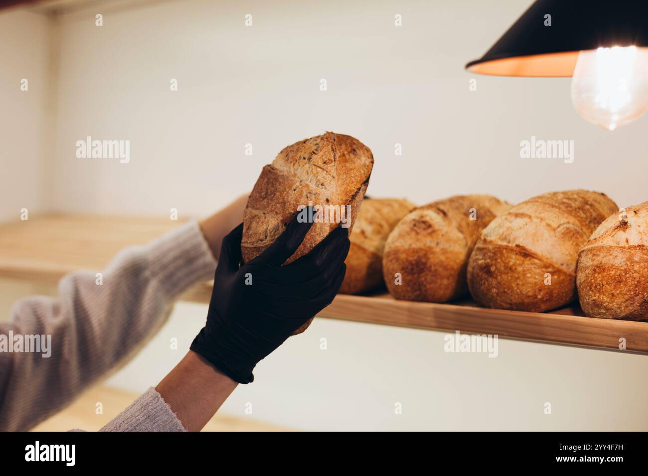 A gloved hand selects a fresh loaf of bread from a wooden shelf in a ...