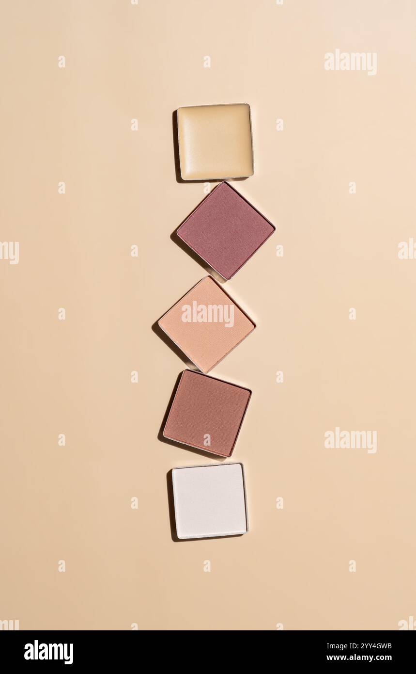 A vertical arrangement of five square makeup powder pans on a light ...