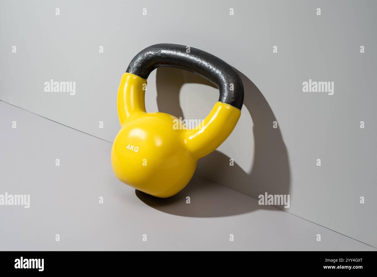 A yellow 4kg kettlebell with a black handle, isolated on a neutral gray ...