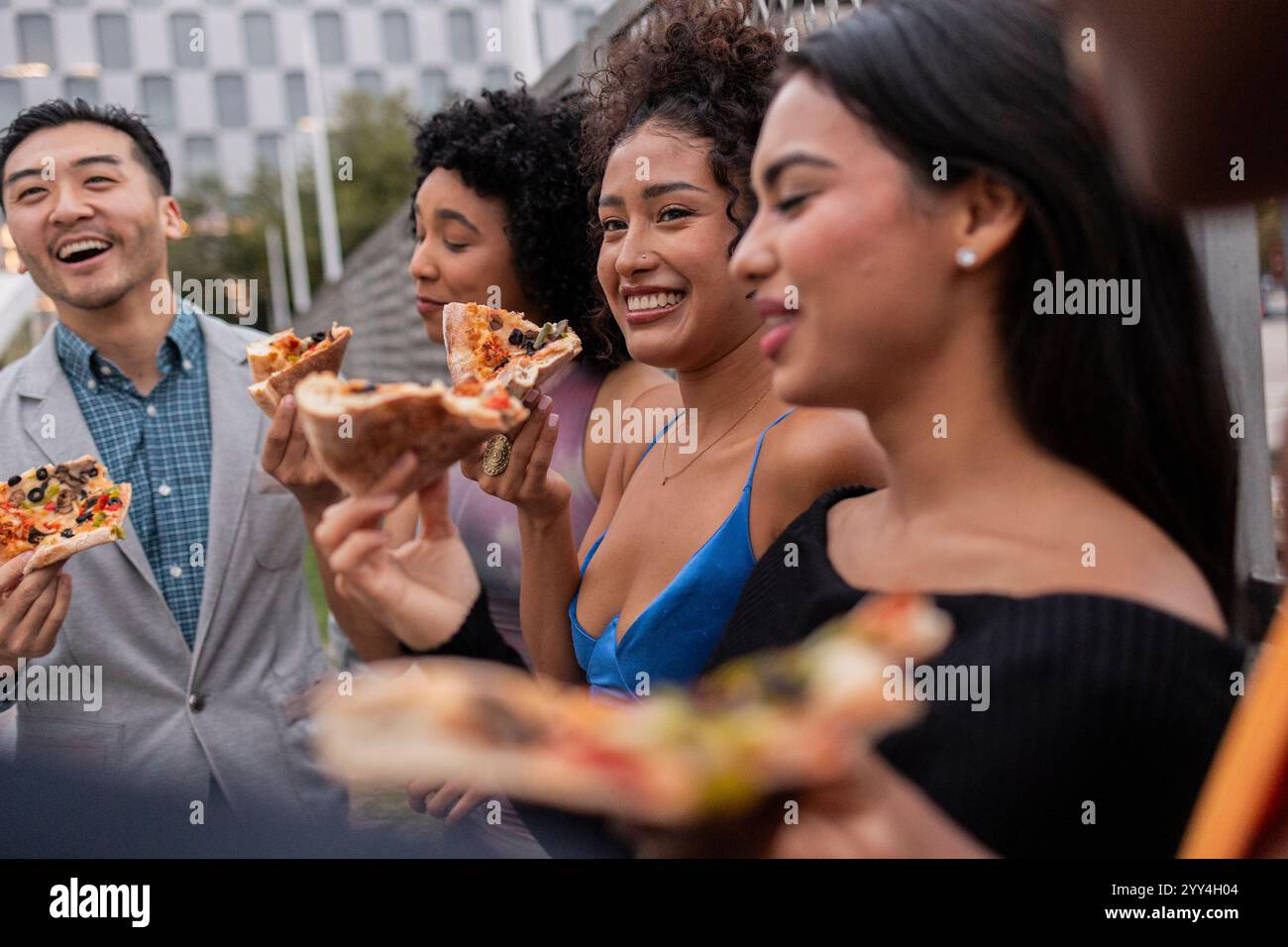 A lively group of friends gathers in an urban setting, enjoying pizza ...