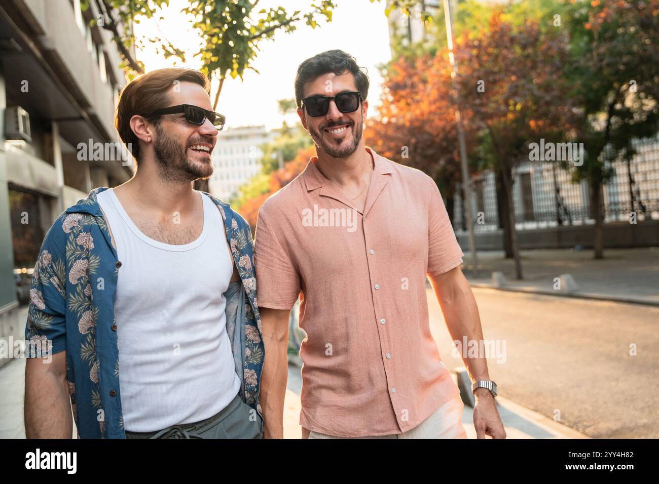 A gay couple walks joyfully along a sunlit city pathway, sharing a ...
