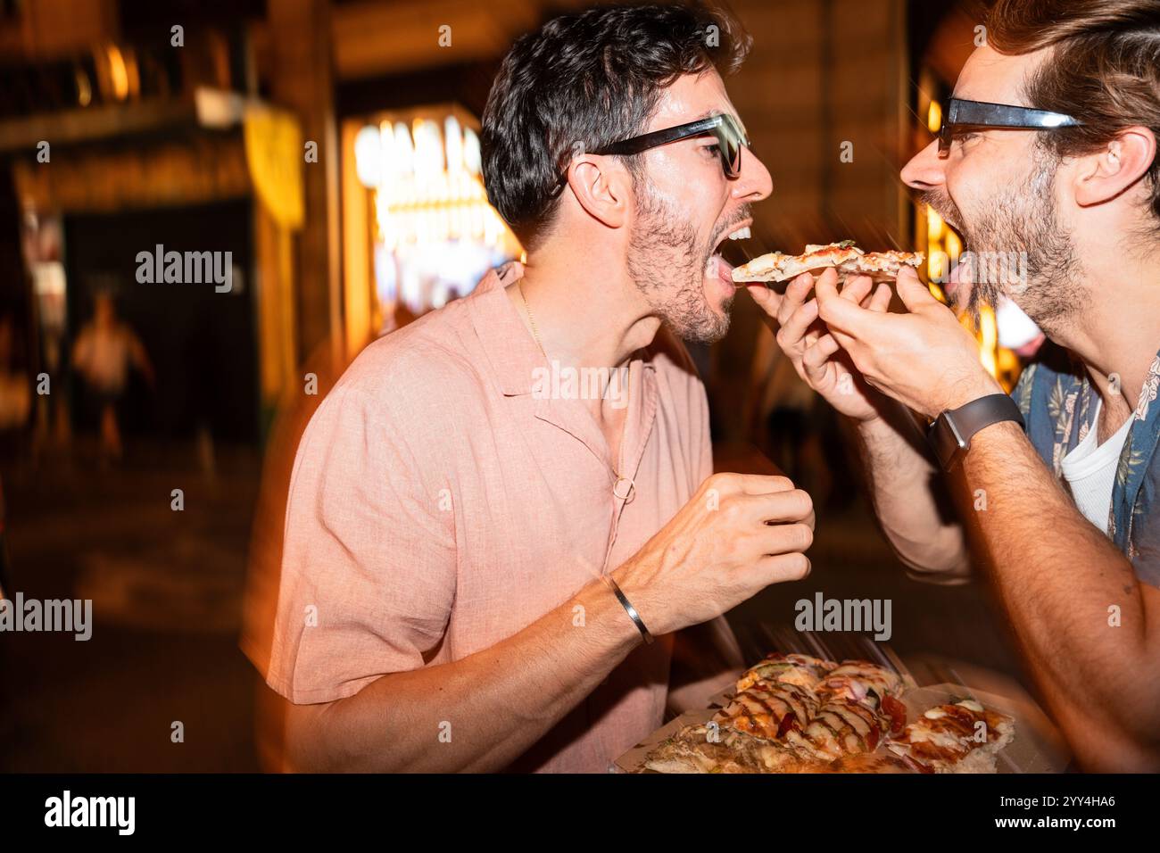 A joyful gay couple shares a slice of pizza during a nighttime outing ...
