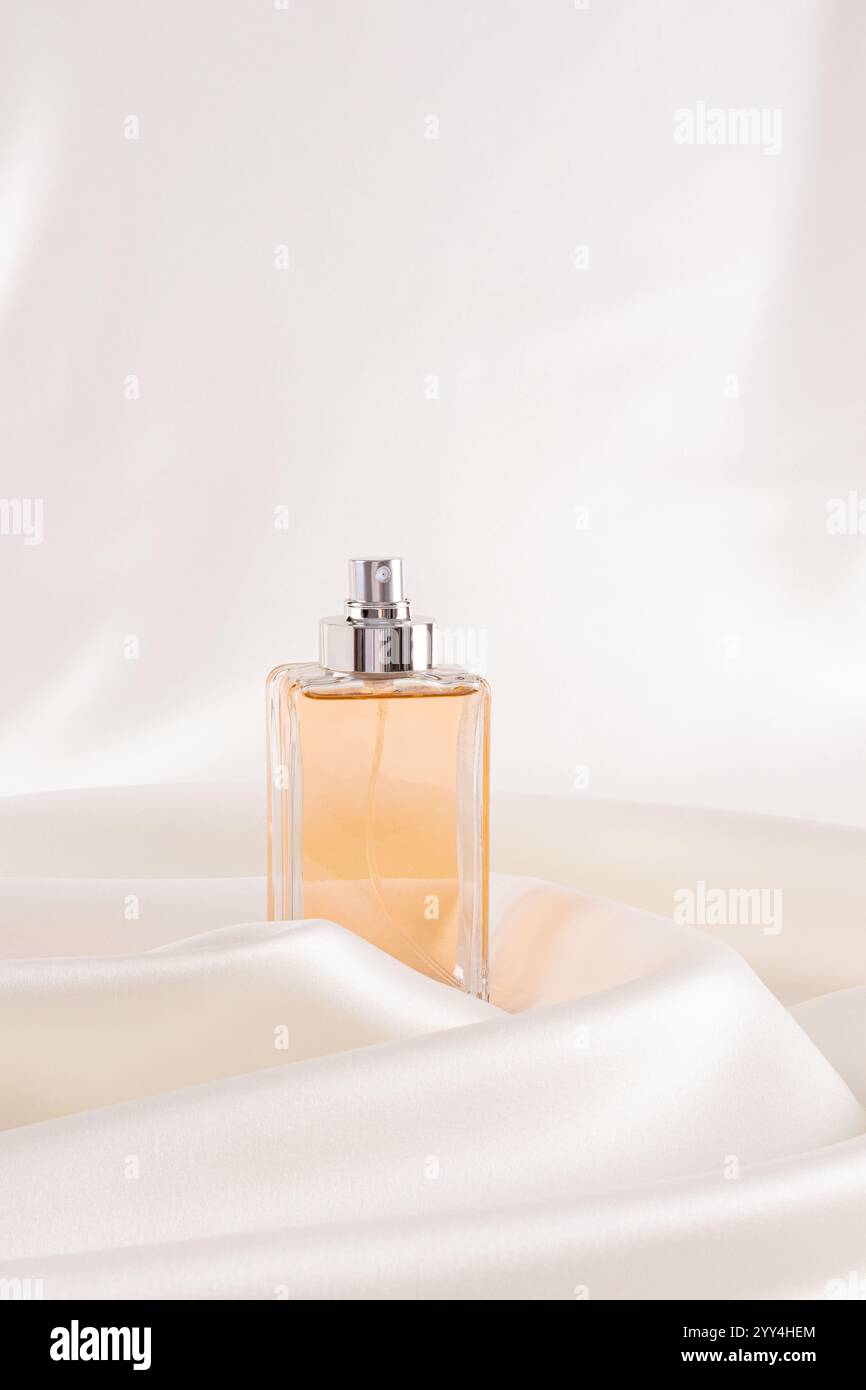 A square perfume bottle sits elegantly on a draped white fabric with ...
