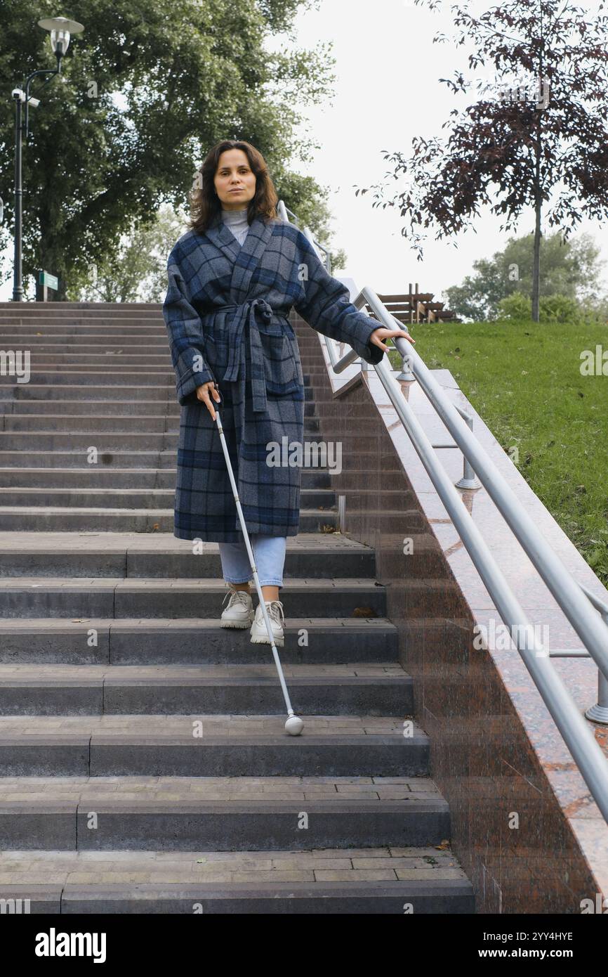 A blind woman wearing a plaid coat uses a white cane to navigate stair ...