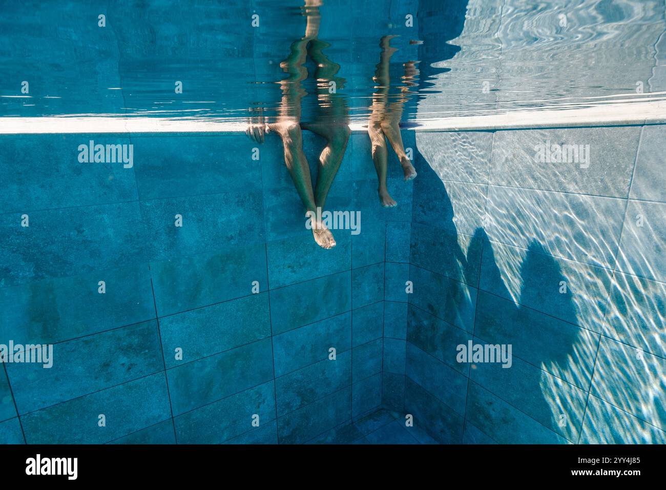 Two people sit on the edge of a swimming pool with their legs submerged ...