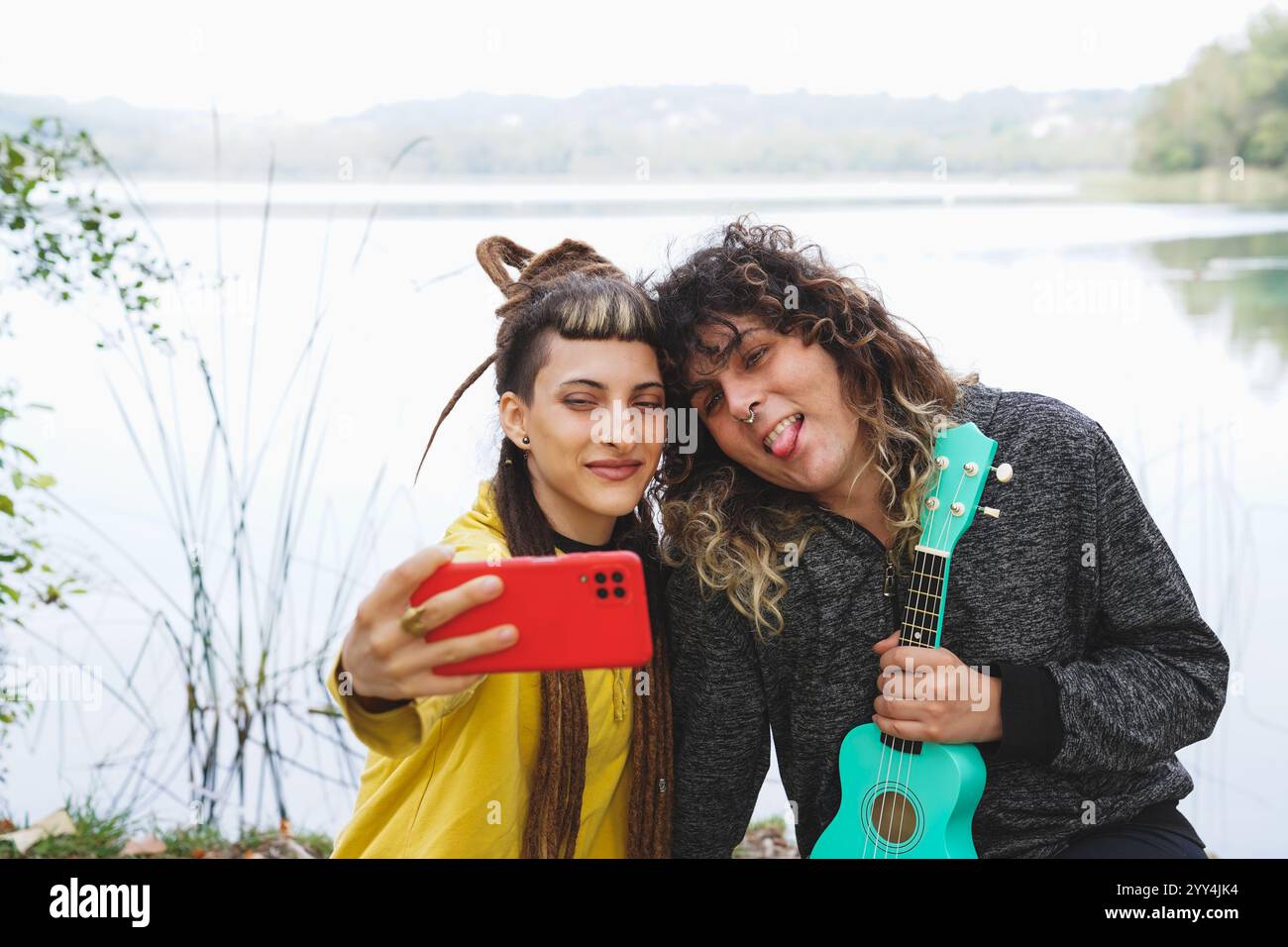 A joyful transgender couple, taking a selfie by a lake. One person ...