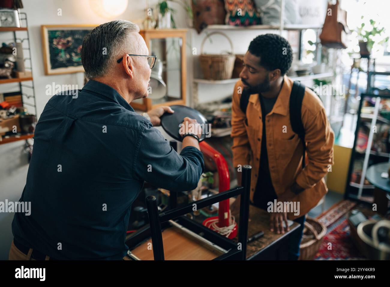 Senior male owner explaining lamp features to customer at antique store ...