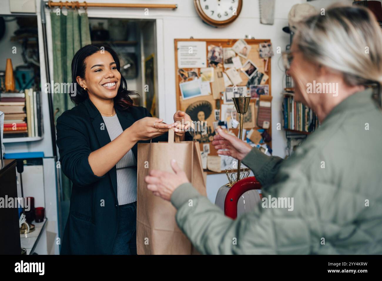Smiling female owner giving paper bag to senior woman at antique store ...