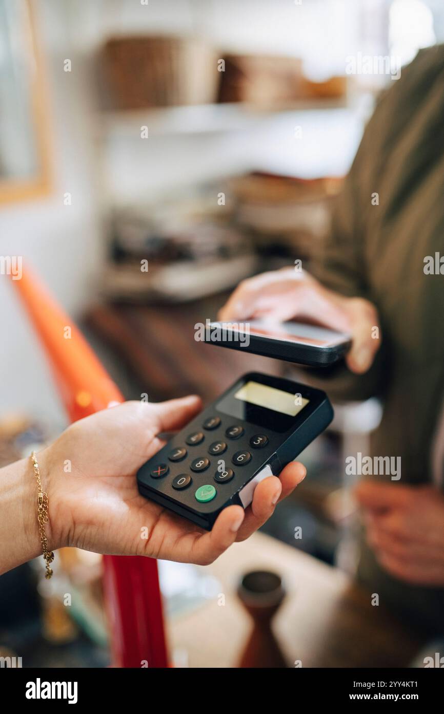 Female owner assisting customer while doing online payment at antique ...