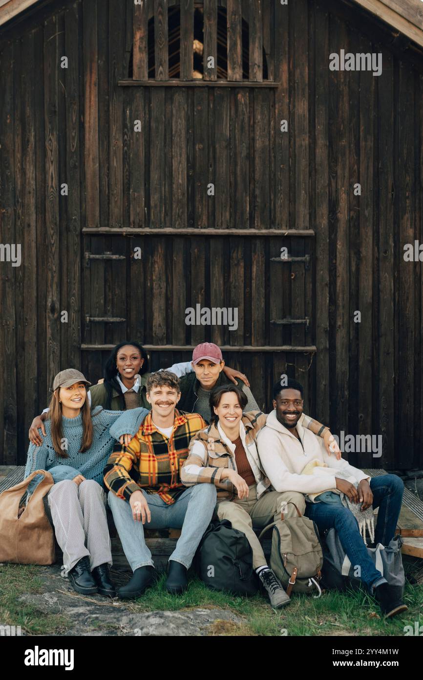 Portrait of happy multiracial male and female friends sitting with arm ...