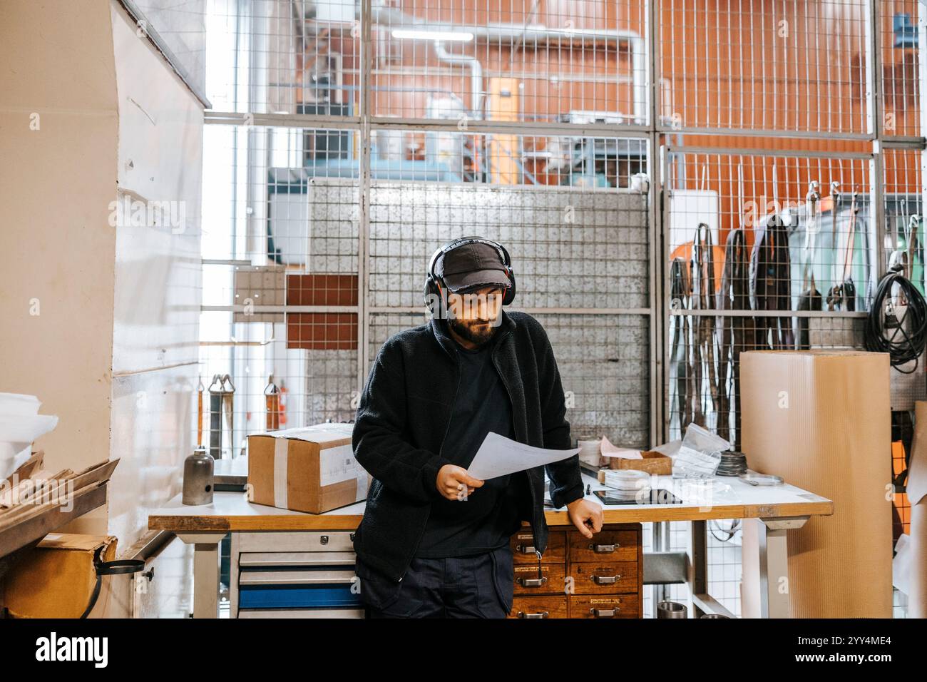 Male employee wearing wireless headphones and cap while reading ...