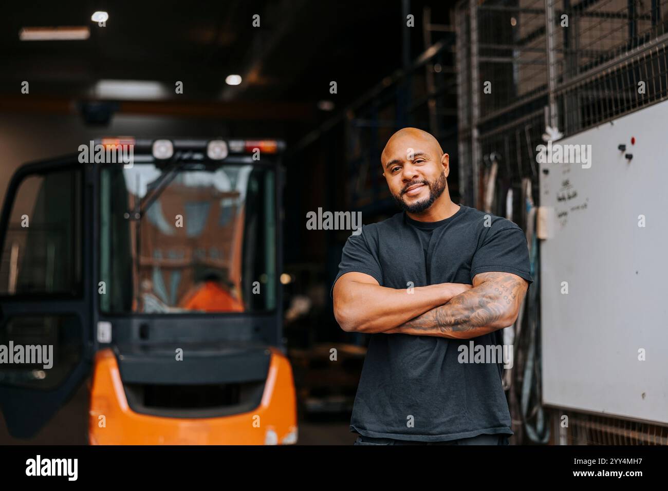 Portrait of smiling bald mature male worker standing with arms crossed ...