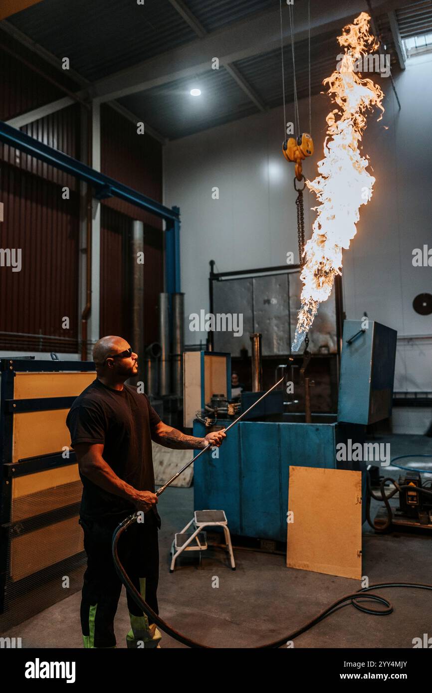Mature male manufacturing expert holding blow torch with fire while standing in factory Stock ...
