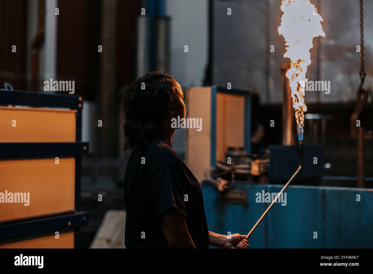 Side view of female manufacturing expert holding blow torch with fire ...
