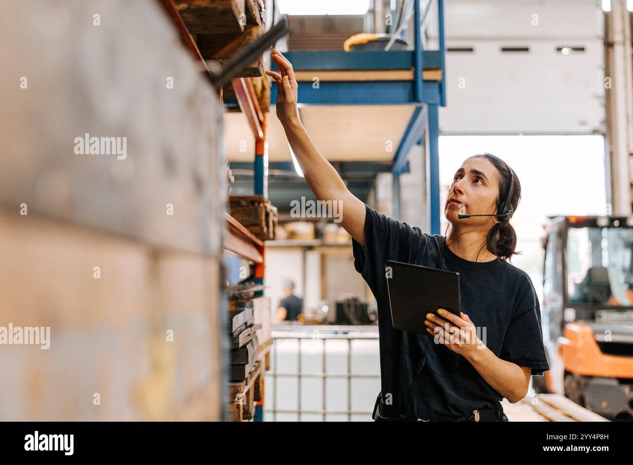 Female worker wearing headset while taking inventory in distribution warehouse Stock Photo - Alamy