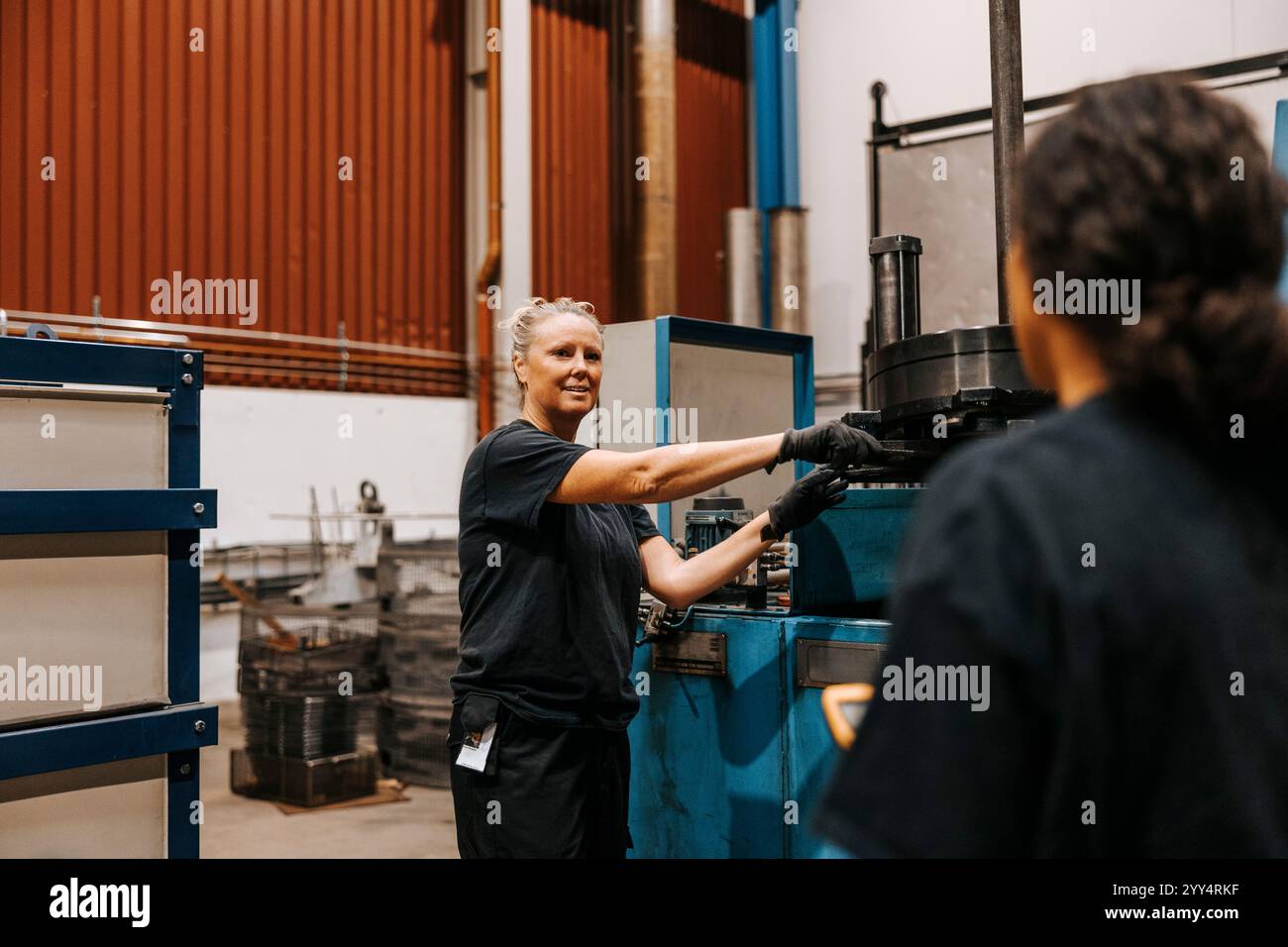 Female worker wearing gloves while working on machine and talking with ...