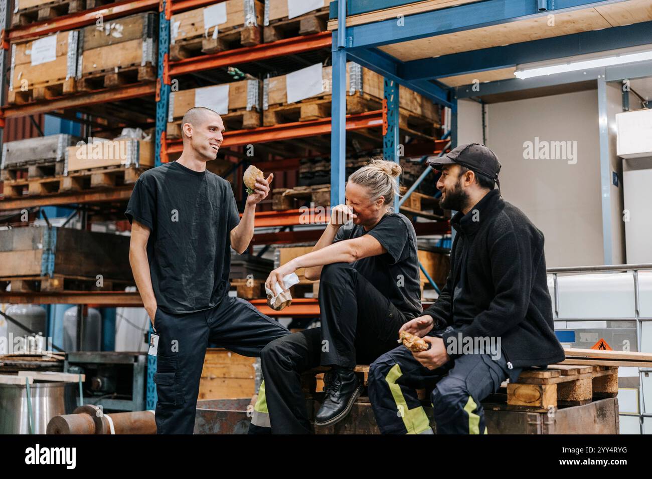 Male and female warehouse workers eating burgers while enjoying and ...