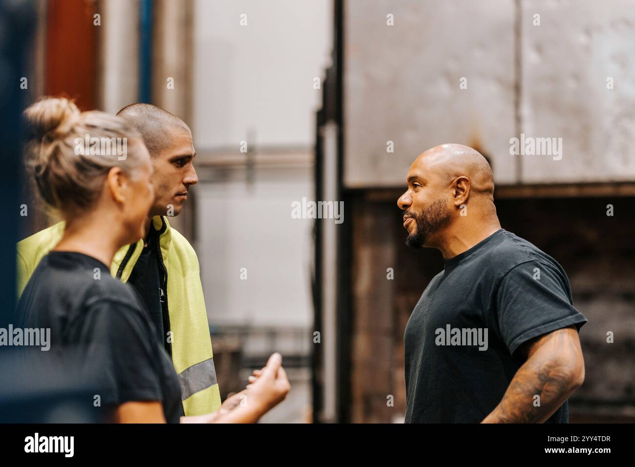 Bald worker discussing with female and male colleague at factory Stock ...