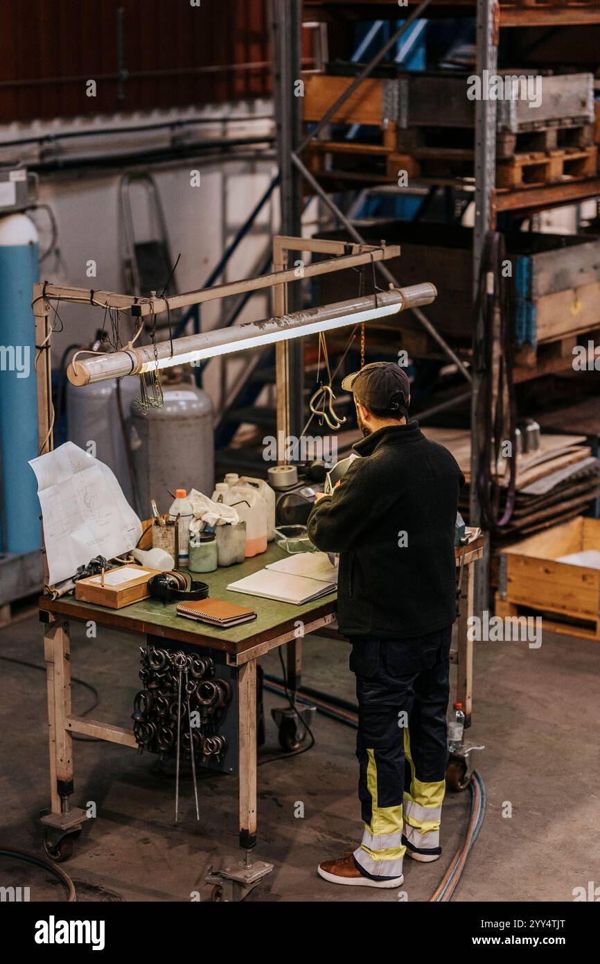 High angle rear view of male worker working while standing near table ...