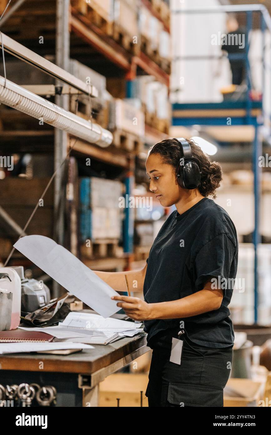 Female employee wearing wireless headphones while reading document near ...