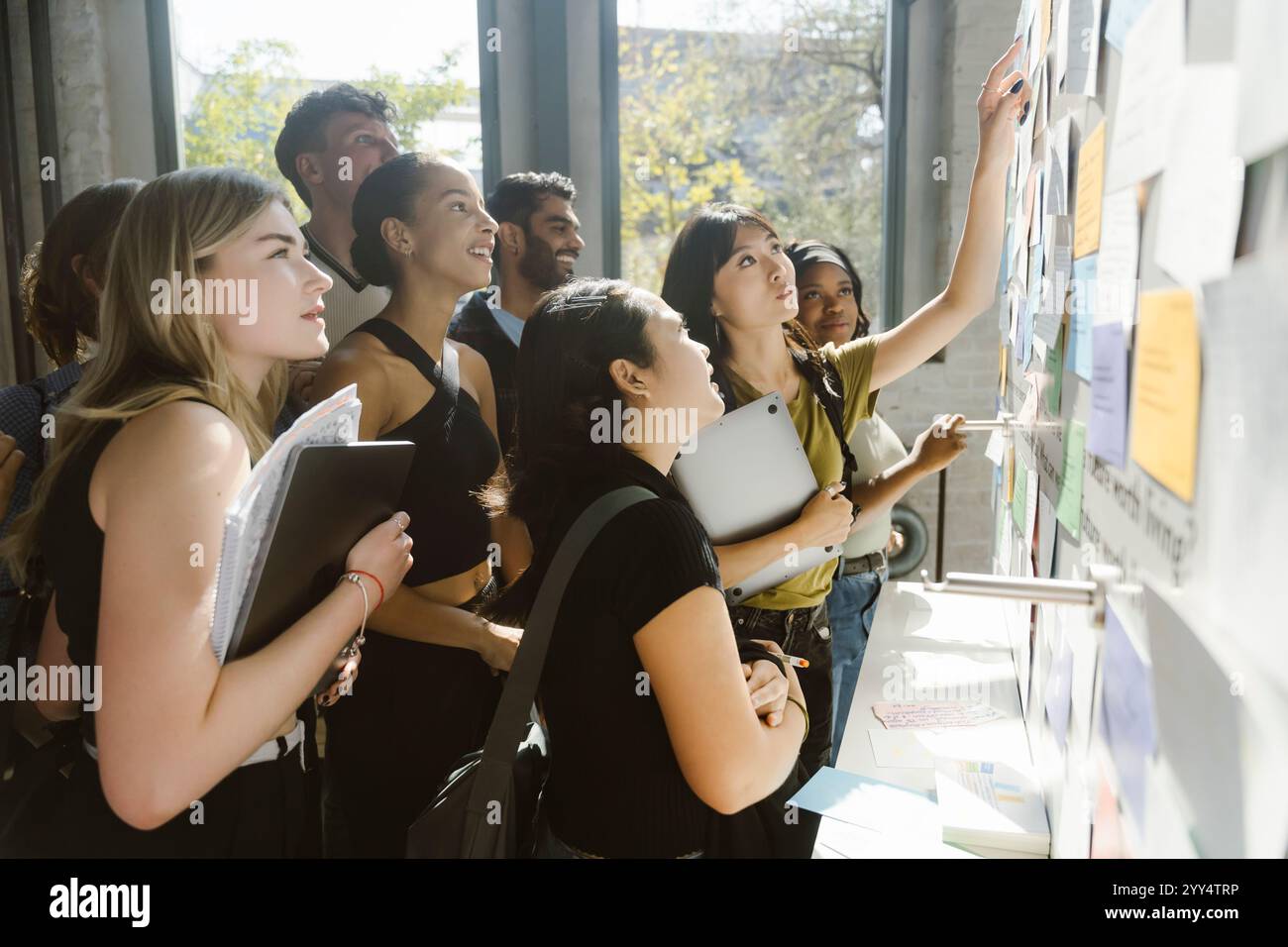 Young woman pointing and reading bulletin board with multiracial ...