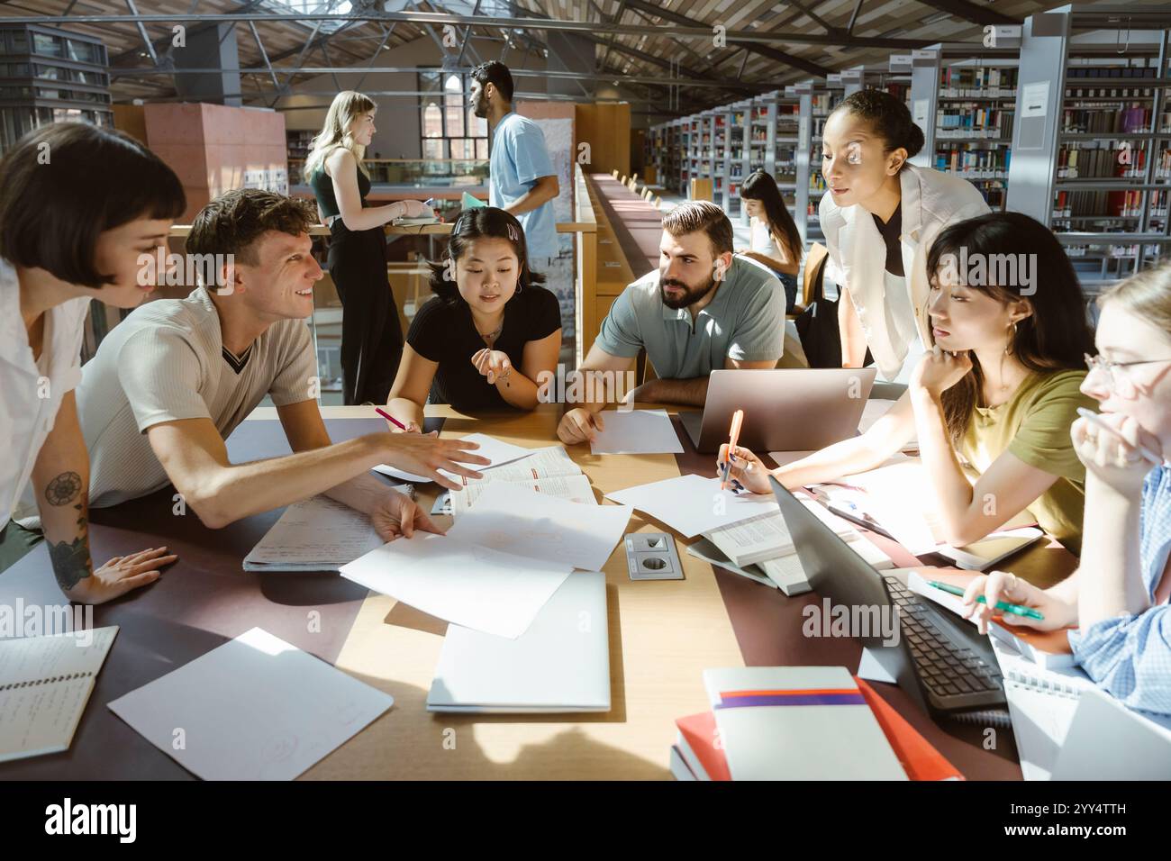 Multiracial male and female students discussing while doing group assignment in library at ...