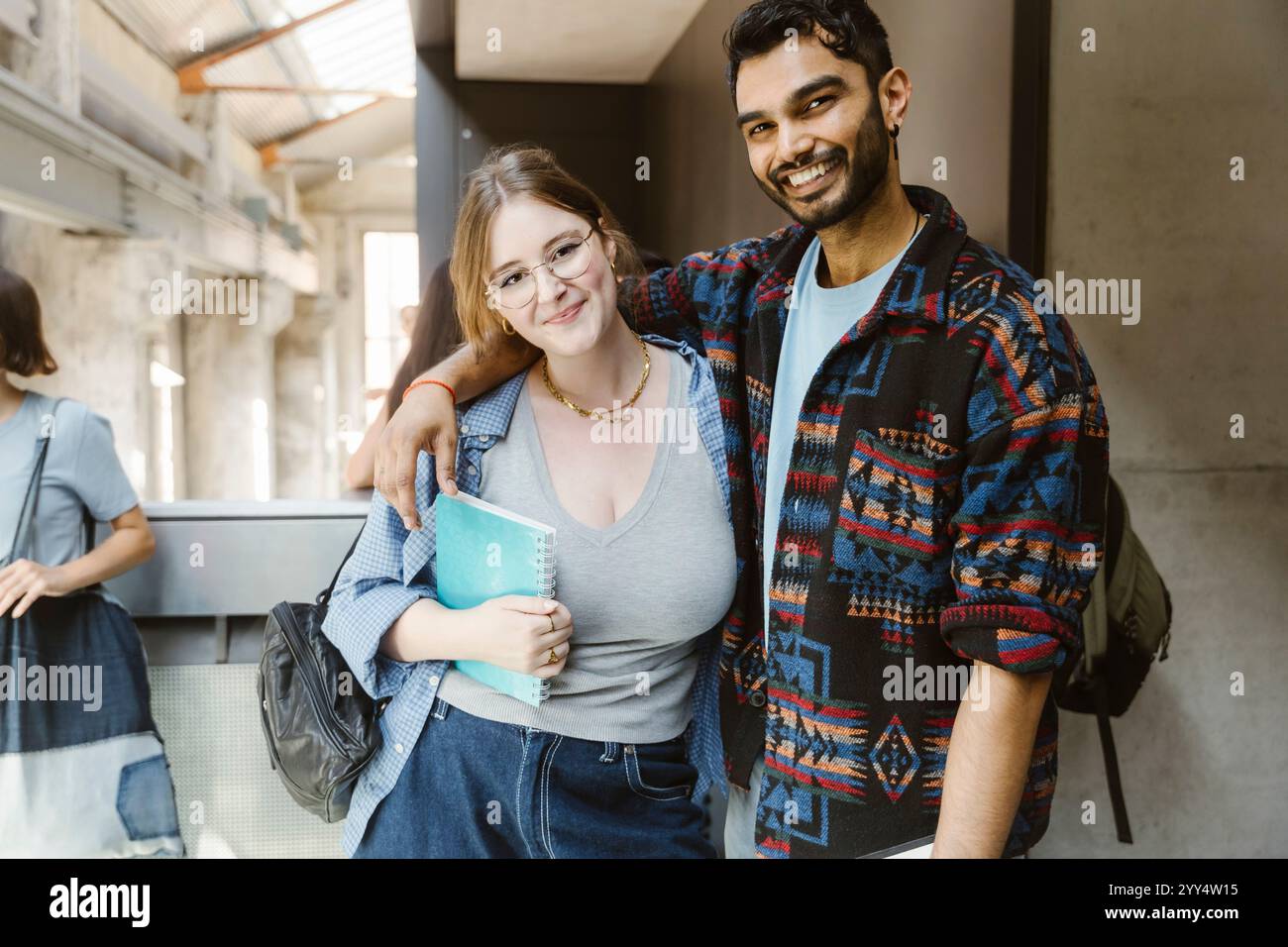 Portrait of happy man standing with arm around female friend at college ...