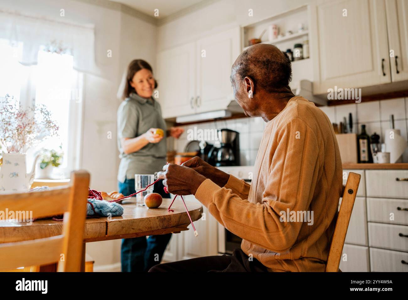 Side view of senior man knitting while talking with female nurse in ...
