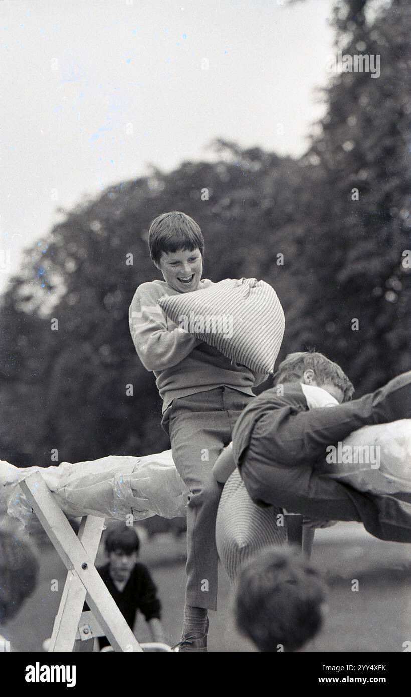 1987, june and outside at a summer fete, two boys on a slippery covered ...