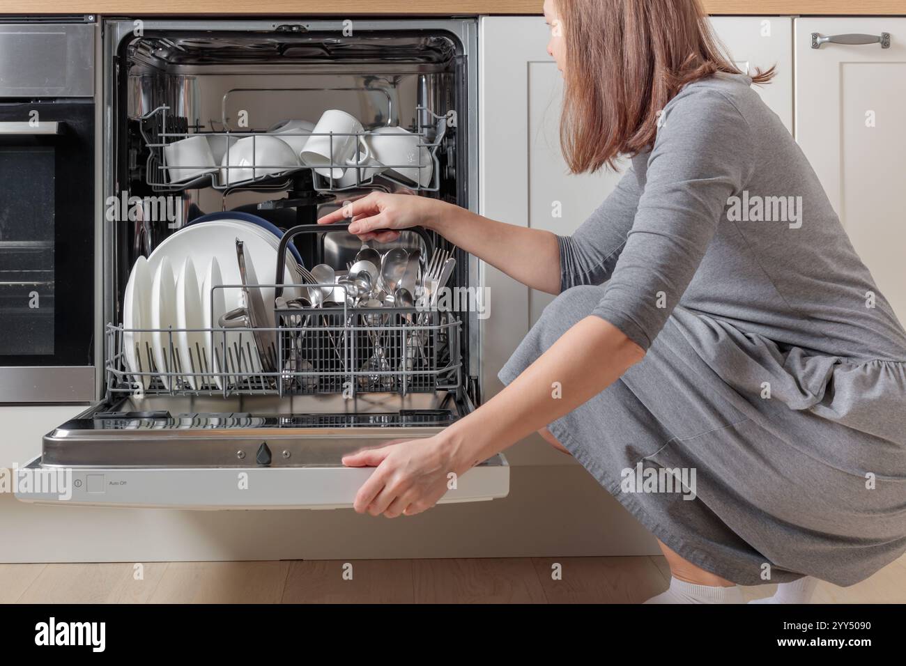 Woman's hands emptying, unloading a dishwasher, taking out a cutlery ...