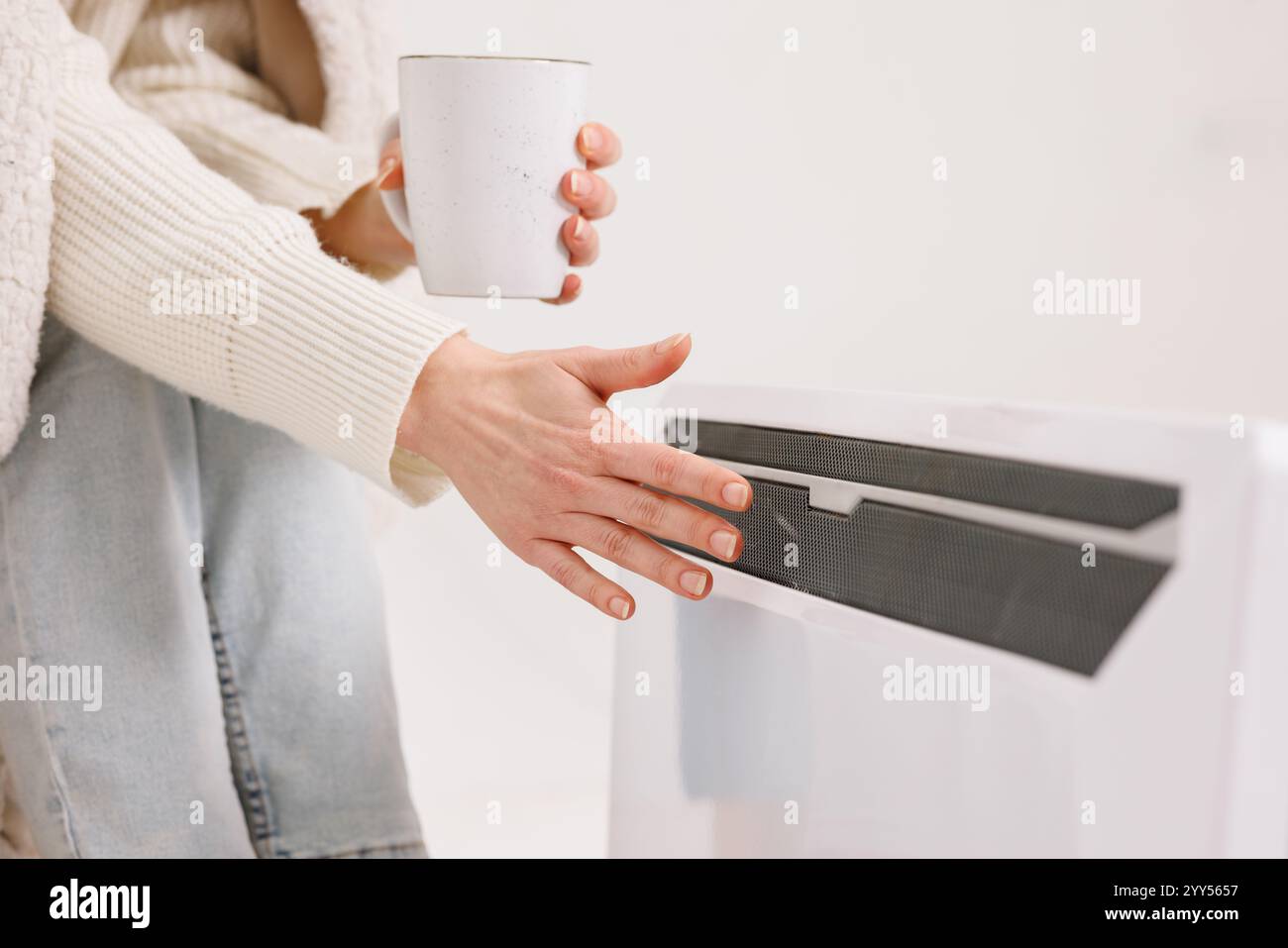 Woman warming hands near electric heater at home. Using heater at home ...