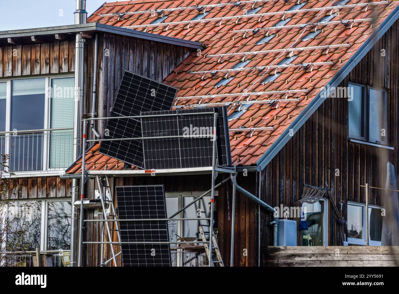 Auf einem Passivhaus aus Holz montiert ein Monteur Solarpanele auf dem ...