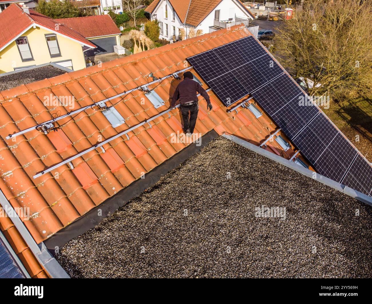 Auf einem Passivhaus aus Holz montiert ein Monteur Solarpanele auf dem ...