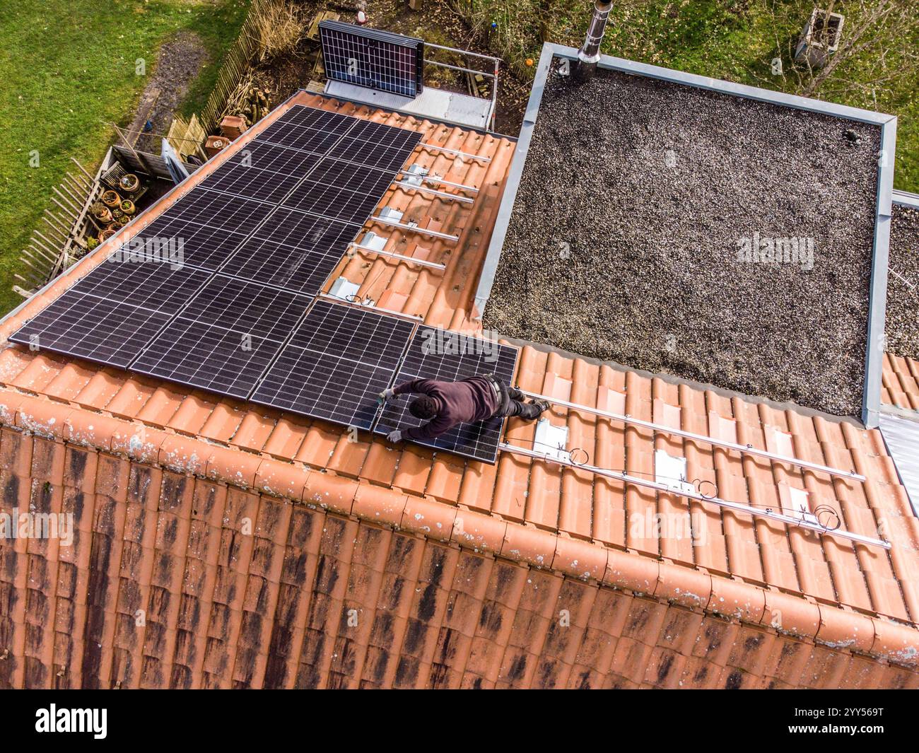 Auf einem Passivhaus aus Holz montiert ein Monteur Solarpanele auf dem ...