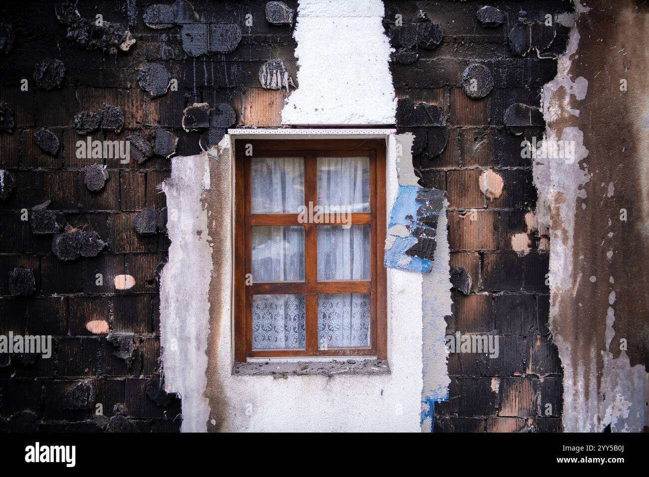 Old vintage wooden window with white curtains on burned out facade. Soot and char around window ...