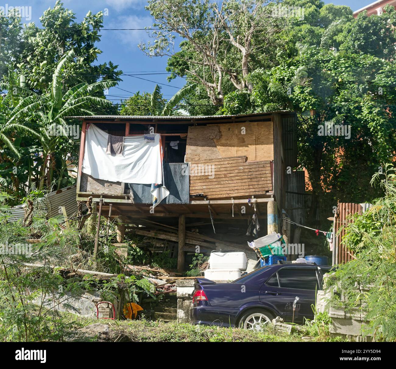 house, on stilts, falling apart, lived in, plywood, fabric hanging, car ...