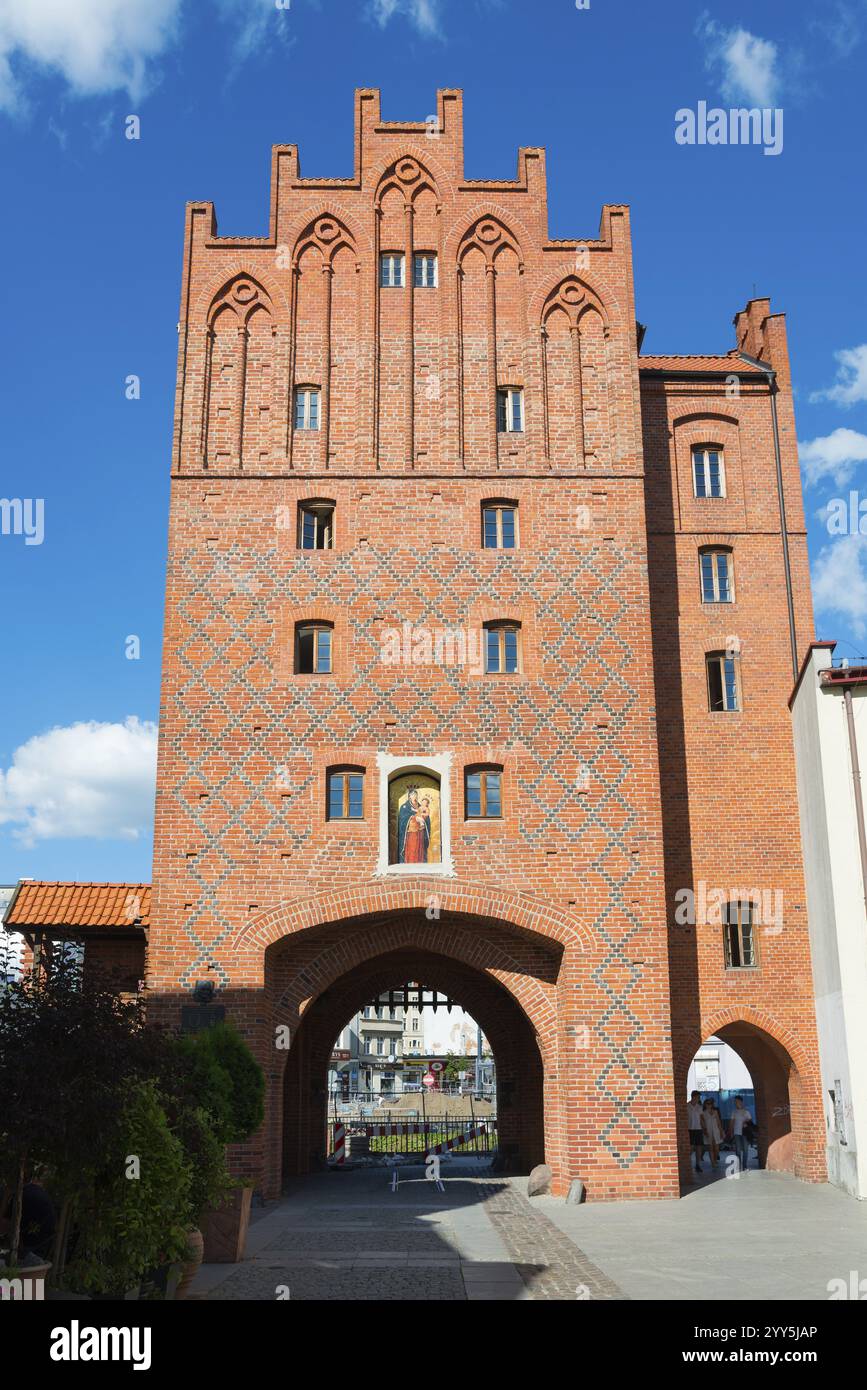 A large Gothic gate made of red brick with ornate patterns under a blue ...